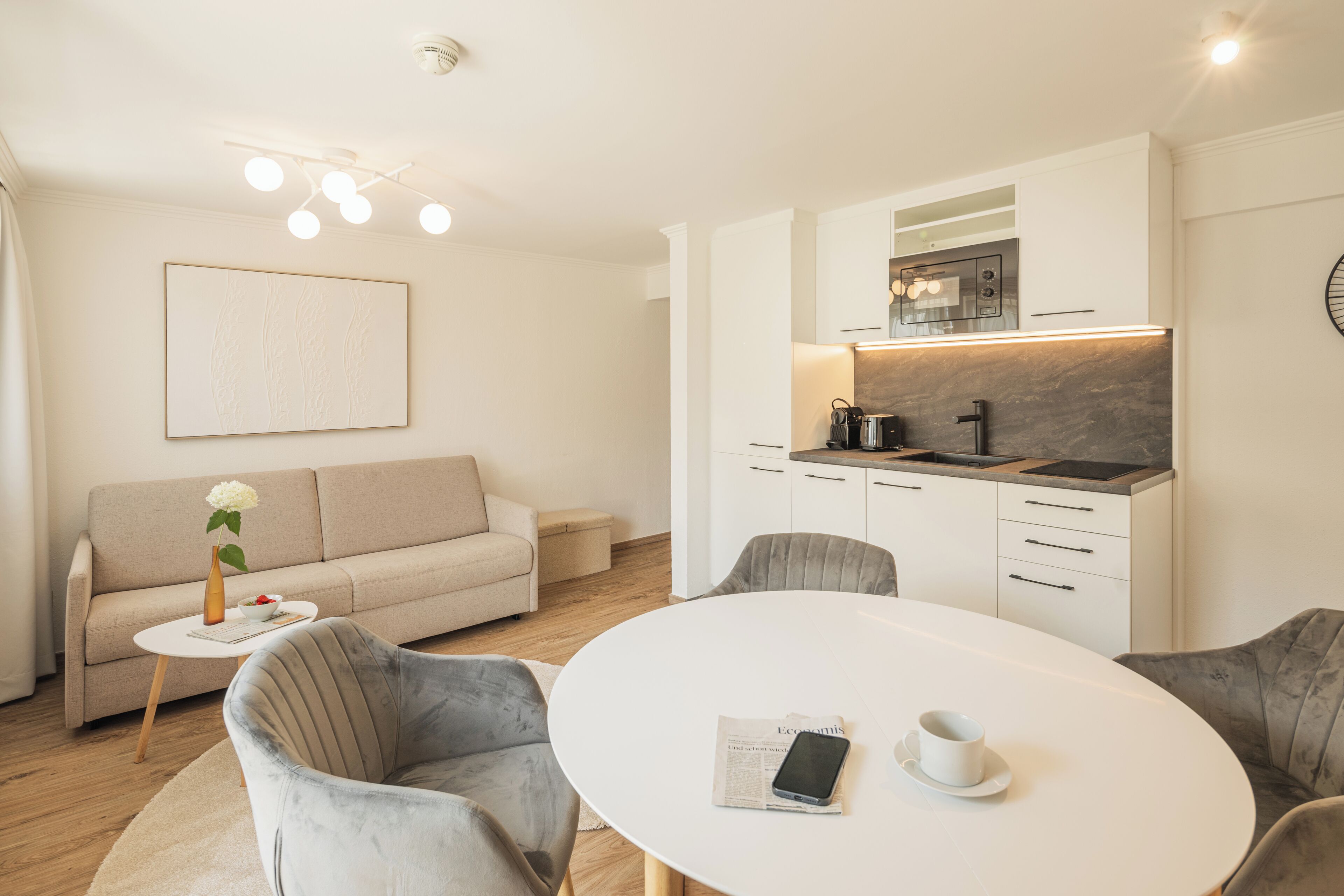 Uma sala de estar moderna com um sofá, uma mesa de jantar redonda e uma cozinha com armários e bancada.