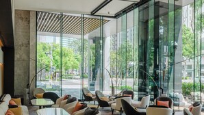Uma área de estar interna moderna, com paredes de vidro, assentos confortáveis e vista para a rua.
