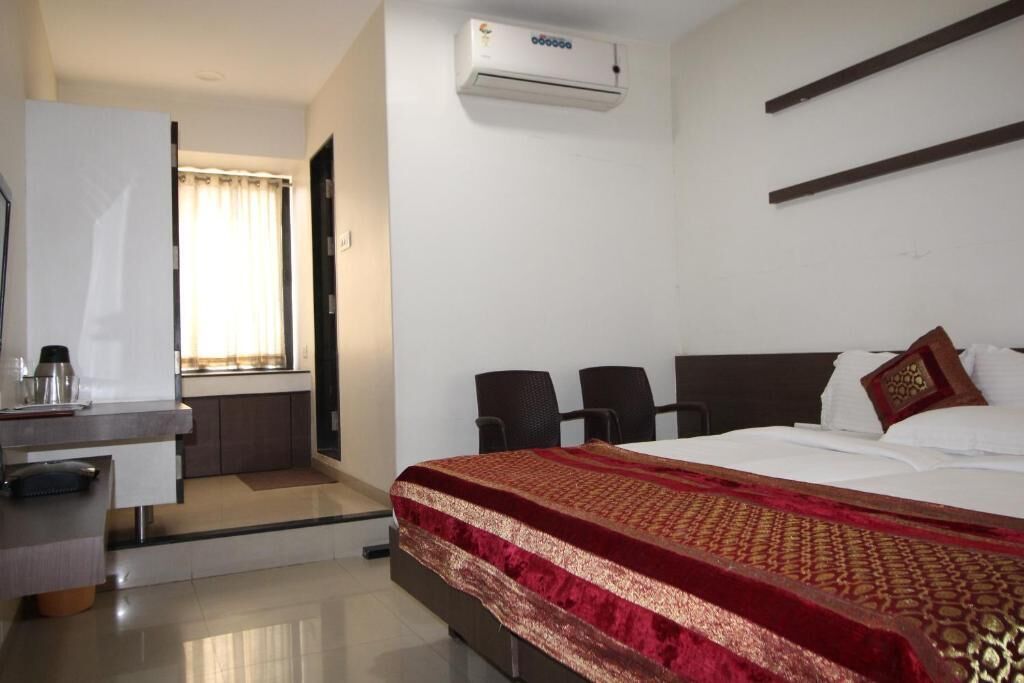 Quarto de hotel com cama, escrivaninha, cadeira, ar condicionado e janela com cortinas.