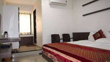 Quarto de hotel com cama, escrivaninha, cadeira, ar condicionado e janela com cortinas.