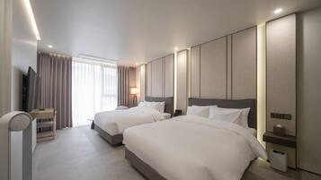 Quarto de hotel com duas camas, televisão, mesa de cabeceira, abajur e janela com cortinas.