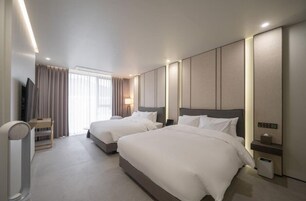 Quarto de hotel com duas camas, televisão, mesa de cabeceira, abajur e janela com cortinas.