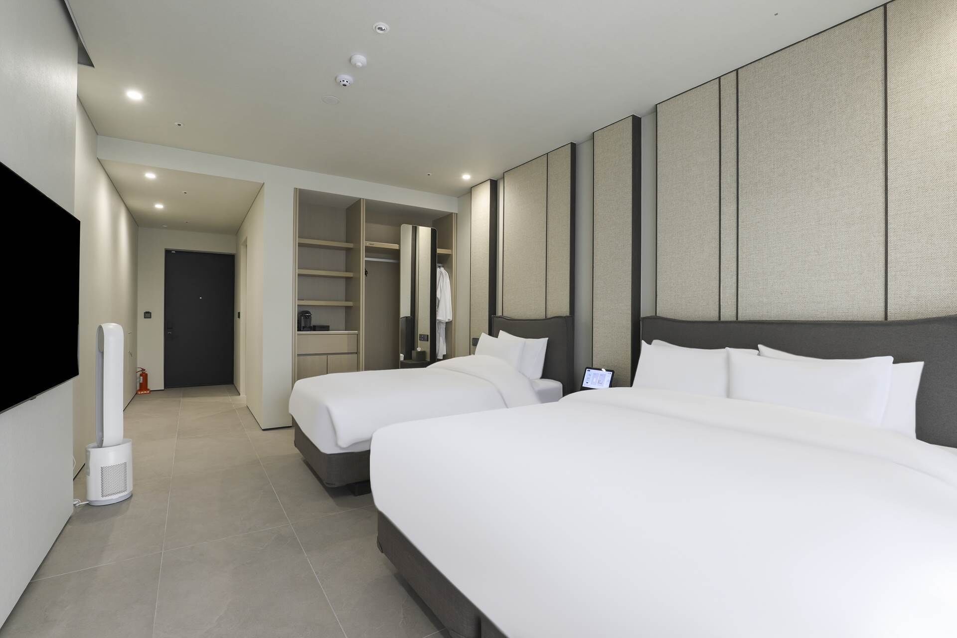 Quarto de hotel com duas camas, um closet espaçoso, um espelho e uma TV de tela plana.