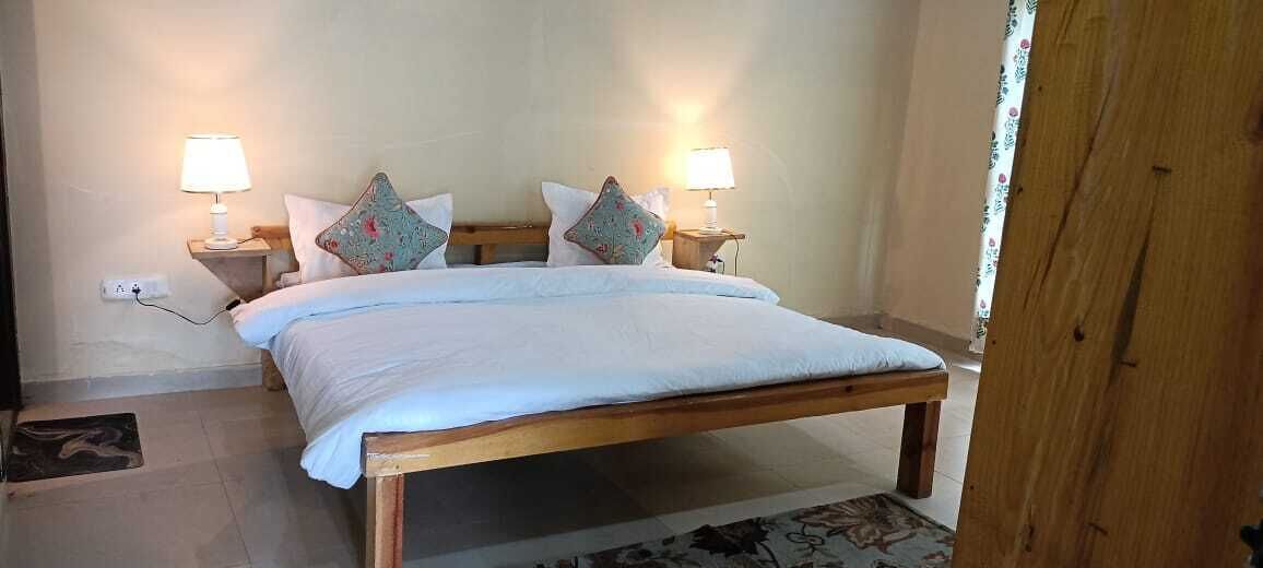 Uma cama de casal com estrutura de madeira, duas mesas de cabeceira com abajures e almofadas estampadas.