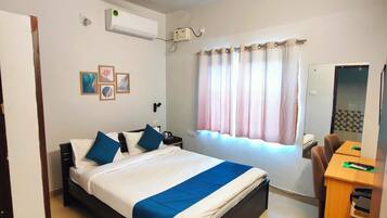 Quarto de hotel com cama, escrivaninha, cadeira, ventoinha no teto e janela com cortinas.