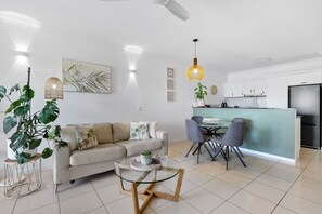 Uma cozinha moderna com armários brancos, uma geladeira preta e uma área de refeições com uma mesa e cadeiras de vidro.