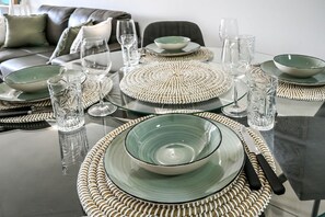 Mesa de jantar posta com pratos verdes, copos transparentes e jogos americanos trançados.