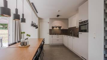 Cozinha moderna com armários brancos, mesa de jantar de madeira e iluminação pendente.