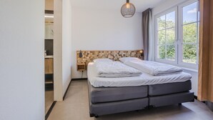 Quarto com cama, mesa de cabeceira, luminária na parede e janela.