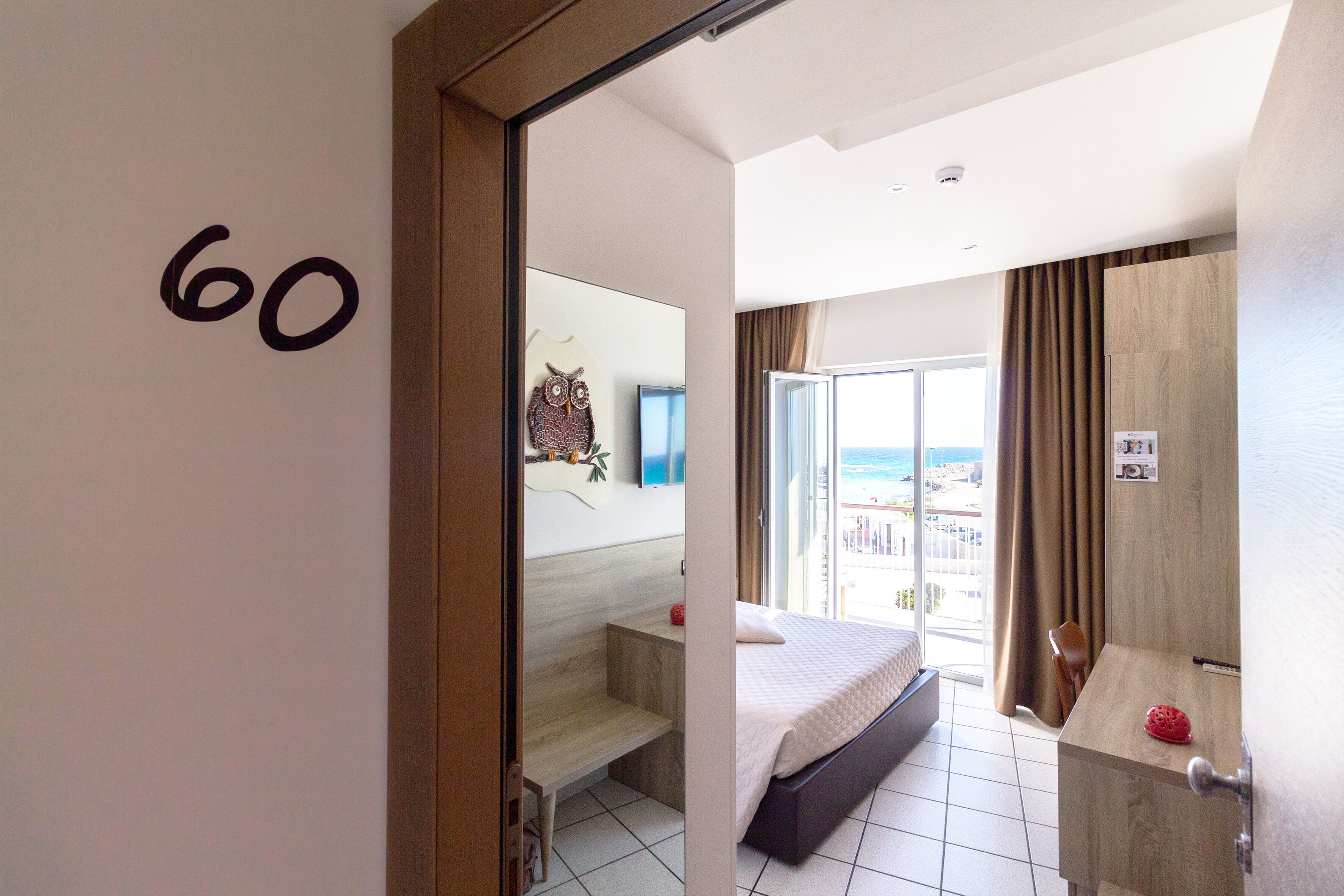 Quarto de hotel com varanda, cama, escrivaninha e vista para o mar.