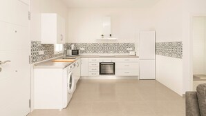 Uma cozinha moderna com armários brancos, máquina de lavar, micro-ondas e geladeira.