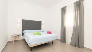 Quarto com cama, mesa de cabeceira e janela com cortinas.