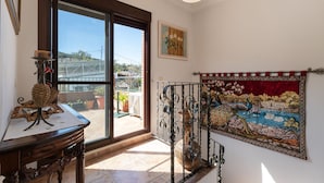 Quarto com uma grande janela, uma mesa com objetos decorativos, tapeçaria e um corrimão com vista para o exterior.