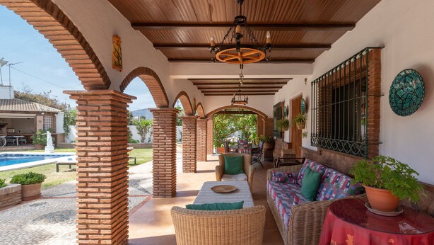 Varanda coberta com móveis de vime, piscina e vista para o quintal.
