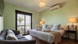 Quarto de hotel com cama, duas mesas de cabeceira com abajures, um sofá e uma janela com grades.