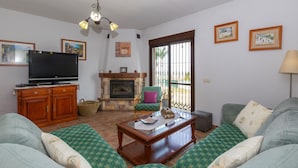 Uma sala de estar com televisão, lareira, sofá verde estampado e um abajur.