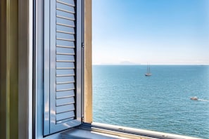 Vista da janela com mar calmo, um veleiro e um pequeno barco a motor.