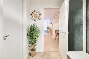 Um corredor com um vaso de planta, um relógio de parede e uma porta que dá para uma sala de jantar.