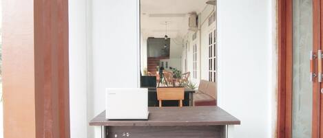 Quarto com escrivaninha, laptop, mesa de madeira e porta com vidro fosco.