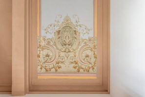 Teto detalhado com padrões ornamentados em dourado e branco, incluindo motivos florais e elementos em espiral.