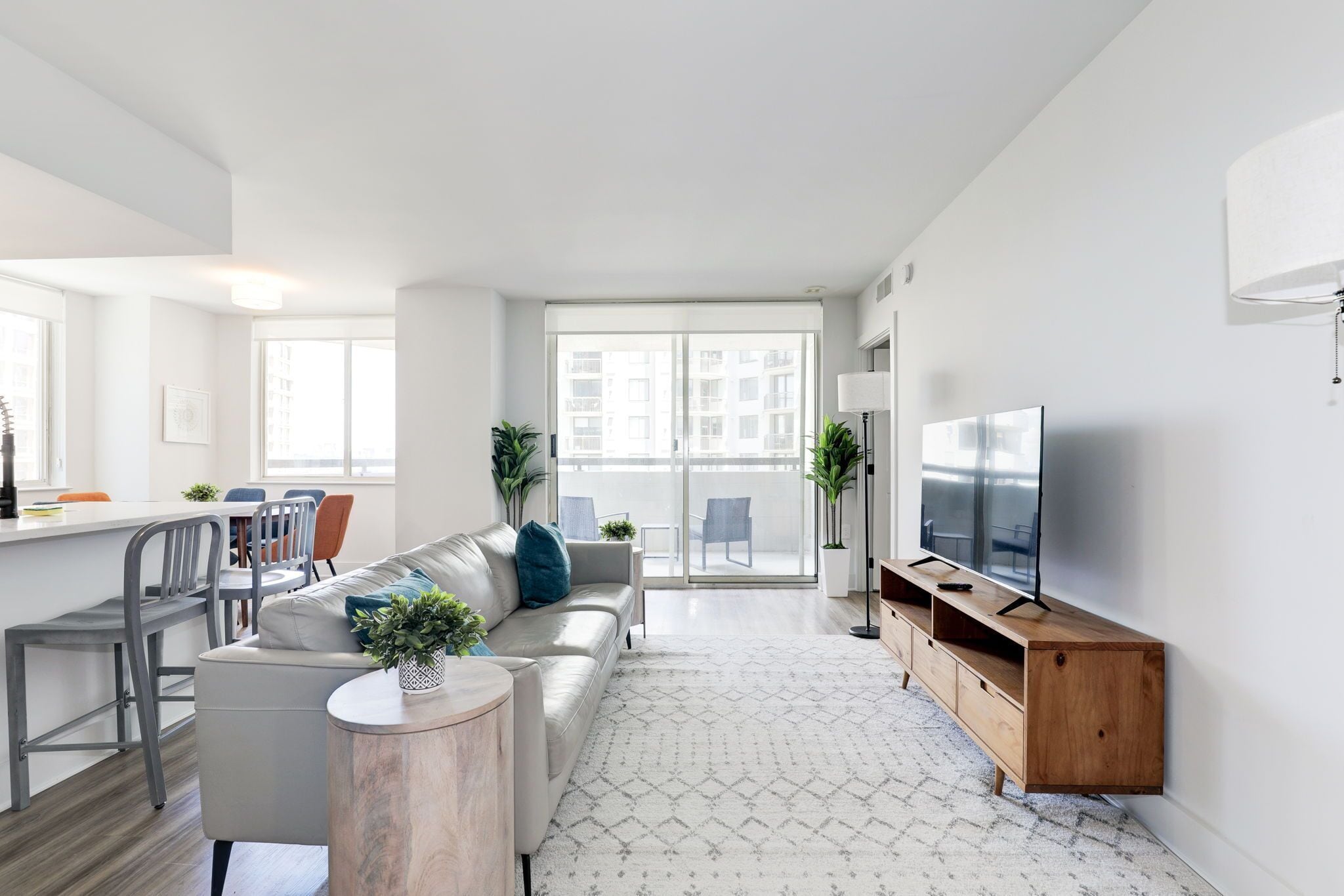 Sala de estar moderna com sofá, mesa de centro e aparador para TV. Há uma área de jantar com cadeiras e mesa, e uma varanda com vista para edifícios.
