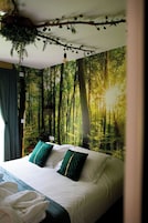 Quarto com cama, almofadas e um mural com tema de floresta na parede.