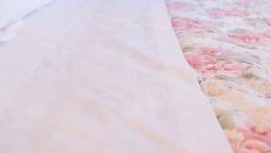 Uma cama com colcha estampada em floral e lençol branco.