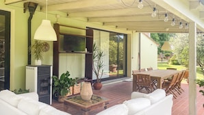 Uma área de varanda coberta com um sofá, uma mesa de madeira e uma televisão fixada na parede.