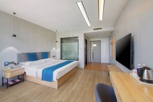 Quarto de hotel moderno com uma cama grande, mesa de cabeceira, televisão de tela plana e escrivaninha com cadeira.