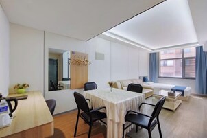 Quarto de hotel moderno com área de refeições, sofá, mesa de centro e uma grande janela com cortinas.