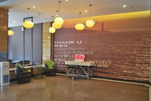 Uma área de recepção com um letreiro 'THANK U', várias luminárias pendentes e uma mesa com um laptop.