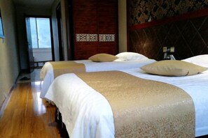 Quarto de hotel com três camas, piso de madeira, parede estampada e vista através de uma porta aberta.