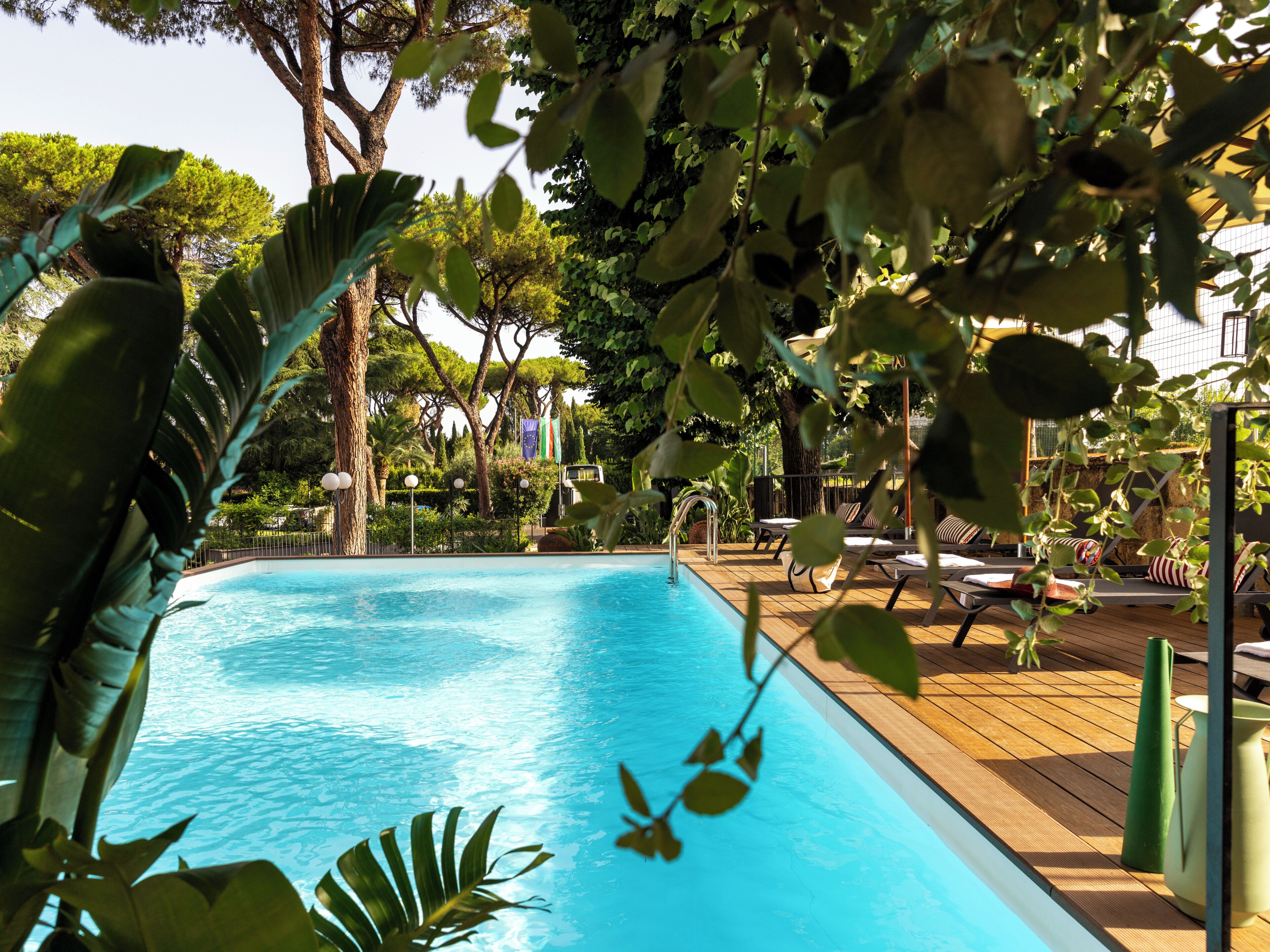 Uma piscina com espreguiçadeiras e guarda-sóis, rodeada por árvores e plantas.