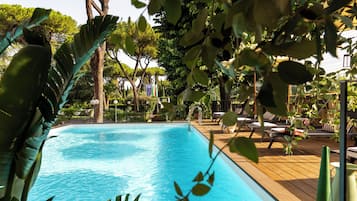 Uma piscina com espreguiçadeiras e guarda-sóis, rodeada por árvores e plantas.