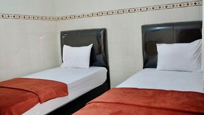 Duas camas de solteiro com cabeceiras pretas e roupa de cama branca, dispostas em um quarto pequeno com paredes revestidas de azulejos e uma moldura decorativa.
