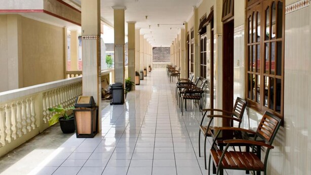 Um corredor com piso de azulejos, bancos de madeira e colunas.