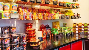 Diversos alimentos embalados em prateleiras e balcão, incluindo lanches, temperos e bebidas.