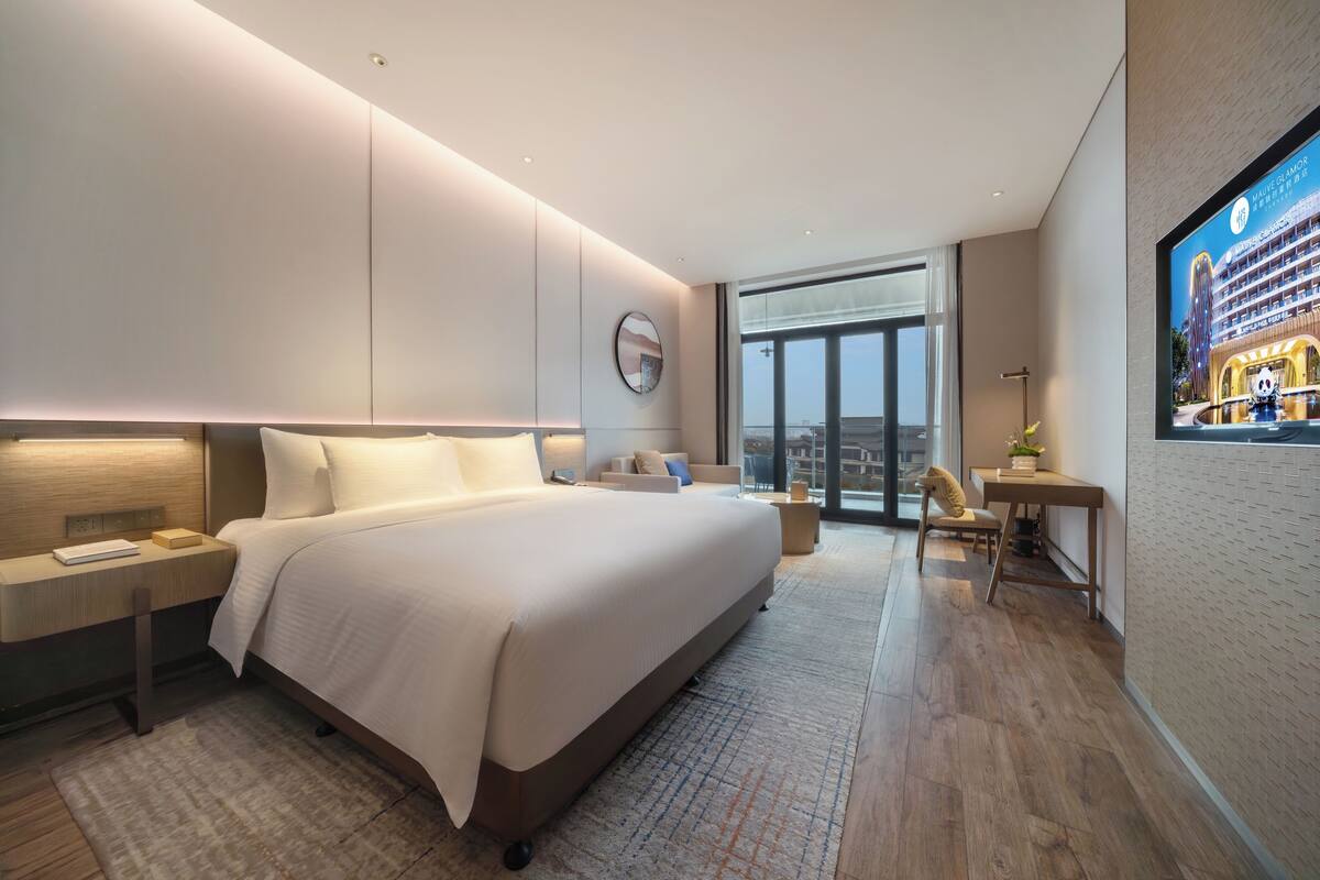 Quarto de hotel moderno com uma cama grande, mesas de cabeceira, escrivaninha e televisão exibindo vista para o hotel.