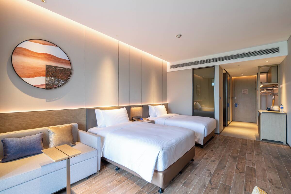 Quarto de hotel moderno com duas camas, um sofá, uma obra de arte redonda na parede e um closet espaçoso.
