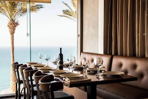 Mesa de jantar posta para seis pessoas, vista para o mar e palmeiras.
