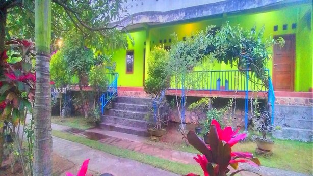 Um edifício com fachada verde vibrante, corrimão azul e escadaria que leva à entrada.
