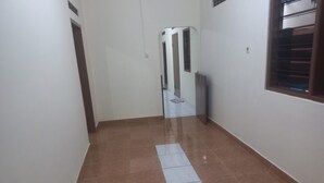 Um corredor com piso ladrilhado, paredes brancas e uma janela com persianas.