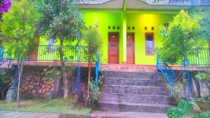 Um edifício com fachada verde vibrante, um conjunto de degraus de concreto levando a uma porta e um corrimão de metal azul.