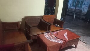 Conjunto de mobiliário de madeira incluindo um sofá, poltrona e mesa de centro, com toalha de mesa estampada sobre a mesa de centro.