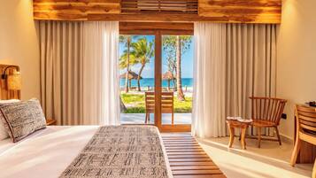 Quarto de hotel com cama, uma cadeira, uma mesa e vista para a praia.