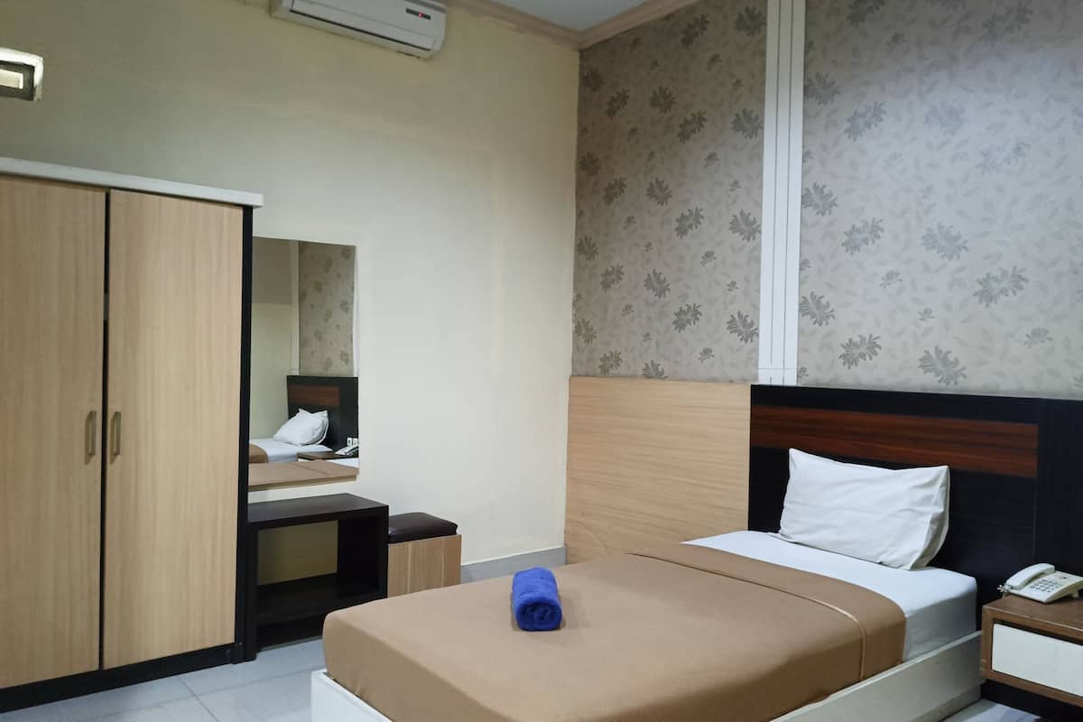 Quarto de hotel com cama, guarda-roupa, mesa de cabeceira, espelho e papel de parede floral.
