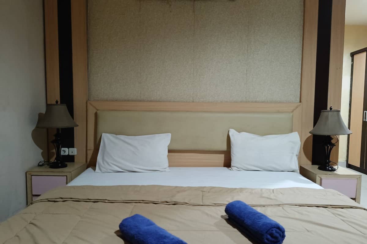 Quarto de hotel com uma cama grande, duas luminárias de cabeceira e uma cabeceira de madeira.