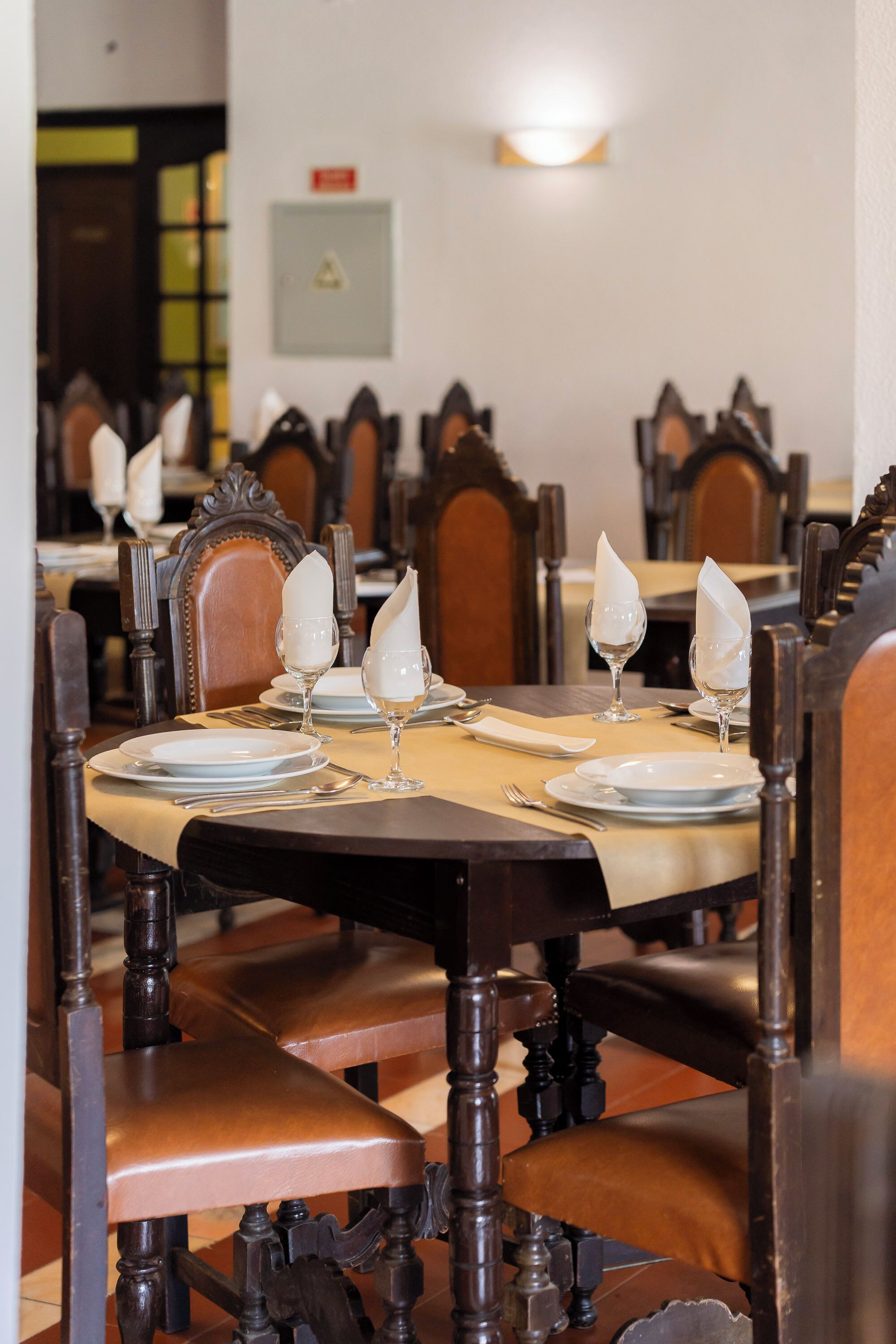 Uma área de refeições com cadeiras e mesas de madeira, cada conjunto com pratos, copos e guardanapos.