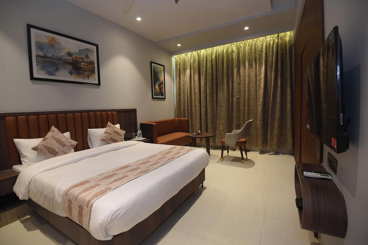 Quarto de hotel com uma cama grande, uma escrivaninha, uma cadeira, uma televisão e um quadro na parede.