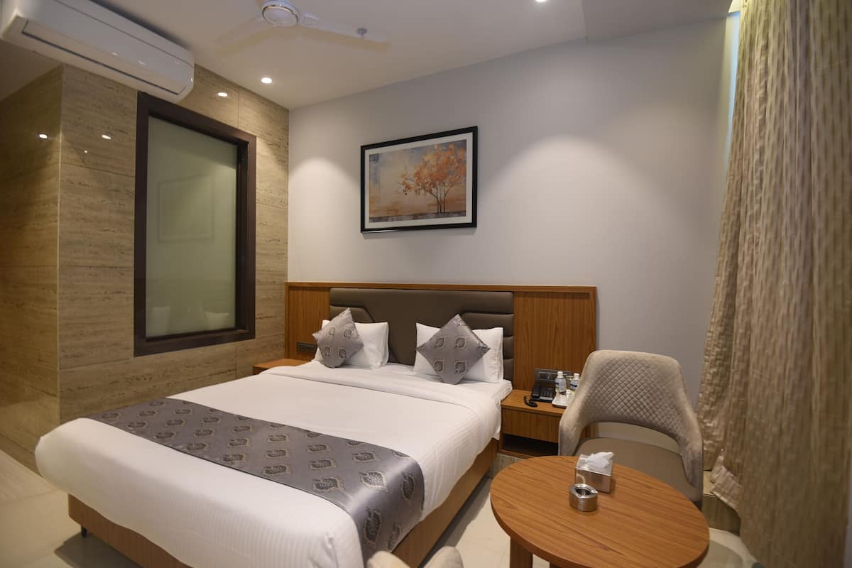 Quarto de hotel com uma cama grande, uma mesa de cabeceira com abajur, uma cadeira e uma mesa redonda.